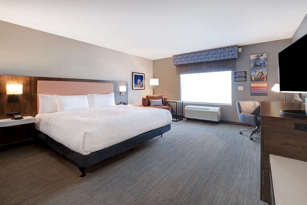 Quarto de hotel com cama grande, escrivaninha, cadeira, televisão e janela.