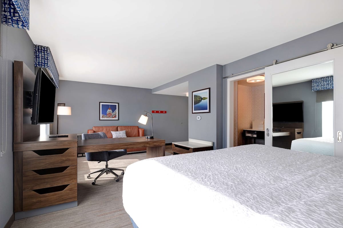 Quarto de hotel com cama, escrivaninha, cadeira e televisão.