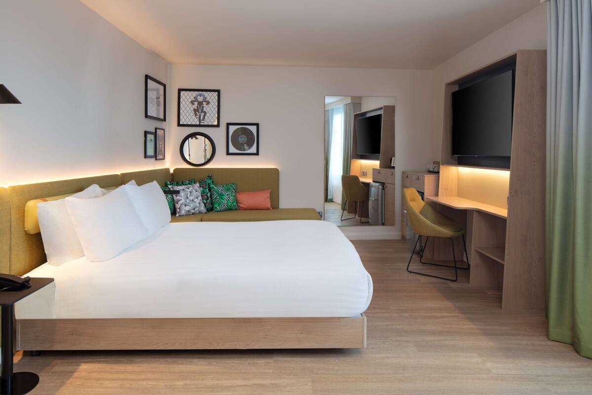 Quarto de hotel moderno com uma cama grande, uma escrivaninha, uma cadeira e uma televisão.