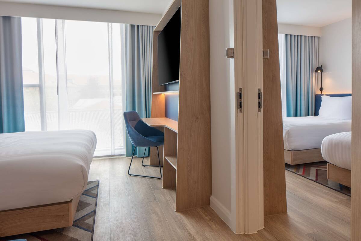 Quarto de hotel com duas camas, uma escrivaninha e uma cadeira.