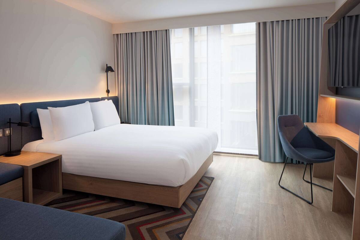 Quarto de hotel moderno com uma cama grande, uma escrivaninha e uma cadeira.