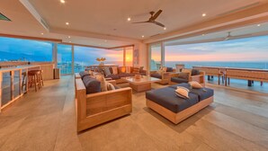 Ampla sala de estar com uma grande janela com vista para o mar, ventilador de teto e espaço para bar.