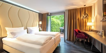 Quarto de hotel com uma cama grande, uma mesa e uma cadeira. Tem uma janela com cortinas e vista para áreas verdes lá fora.