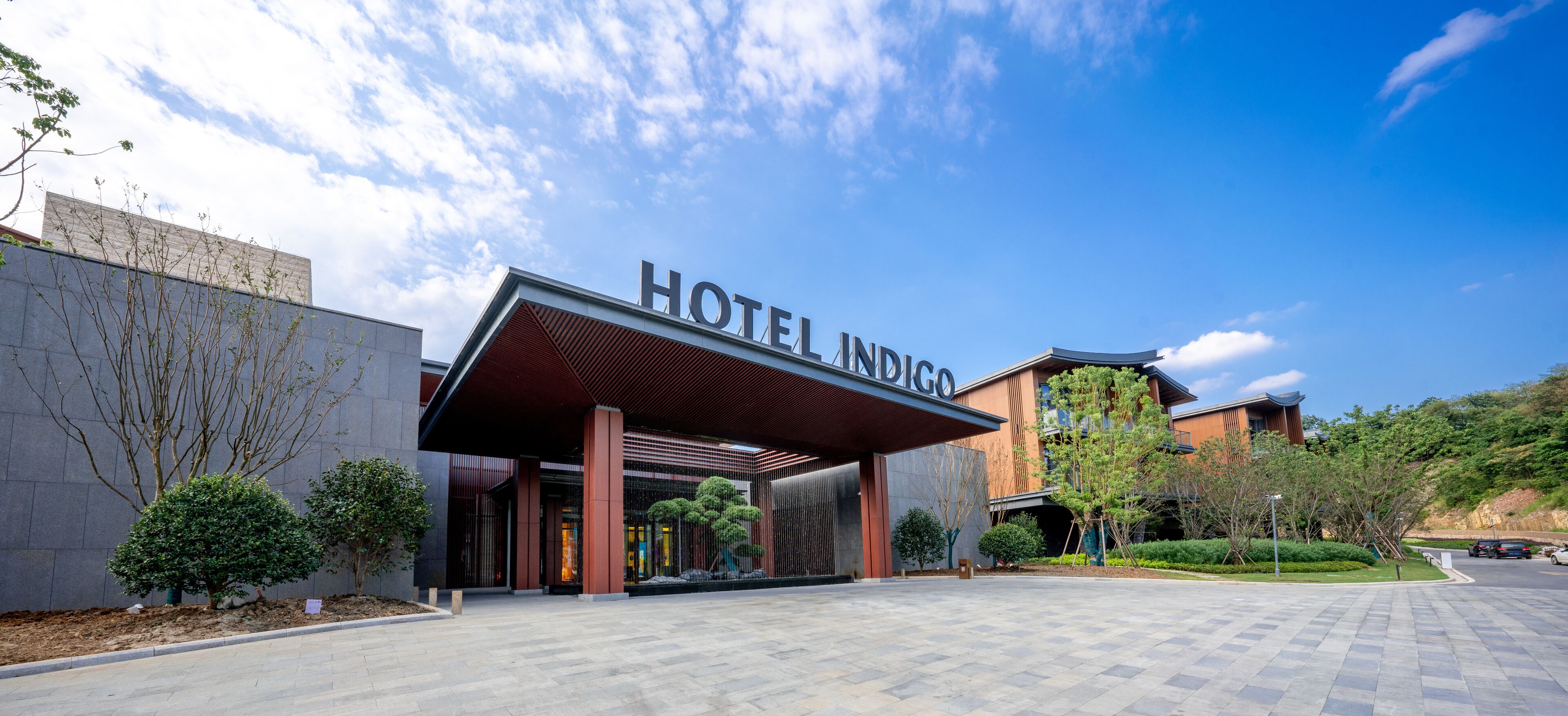 Exterior do Hotel Indigo, com design moderno, destacando uma entrada imponente e um jardim bem cuidado.