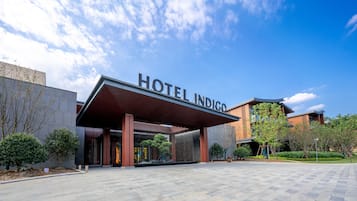 Exterior do Hotel Indigo, com design moderno, destacando uma entrada imponente e um jardim bem cuidado.