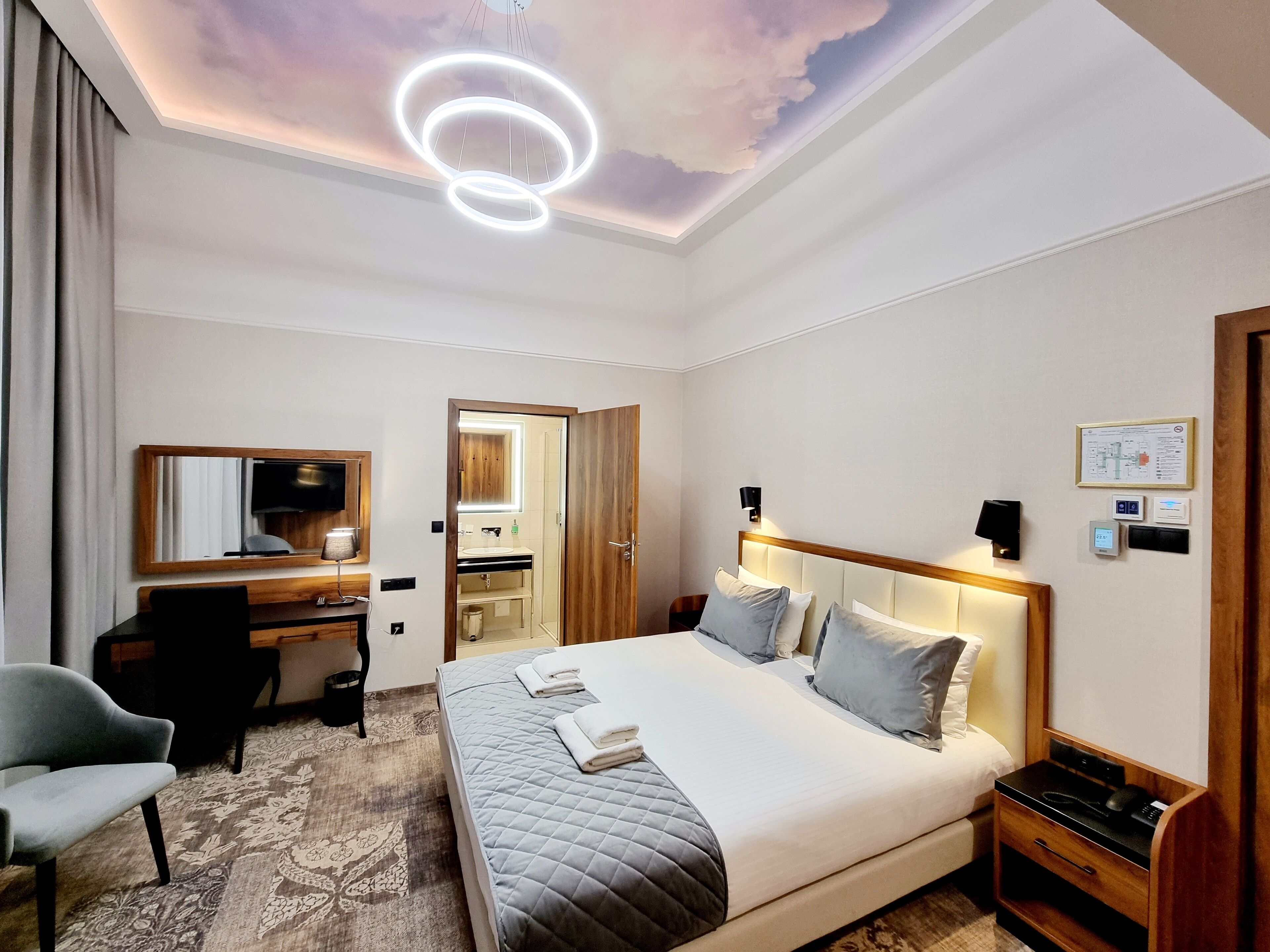 Quarto de hotel com cama, mesa de cabeceira, abajur e teto com desenho de nuvem.