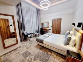 Quarto de hotel com uma cama grande, uma escrivaninha, duas cadeiras, um espelho e uma luminária no teto.