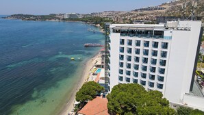 Um hotel alto com piscina e acesso à praia, com vista para uma área costeira de águas cristalinas e barcos.