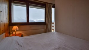 Quarto com uma cama grande, uma mesa de cabeceira com abajur e uma janela com cortinas.