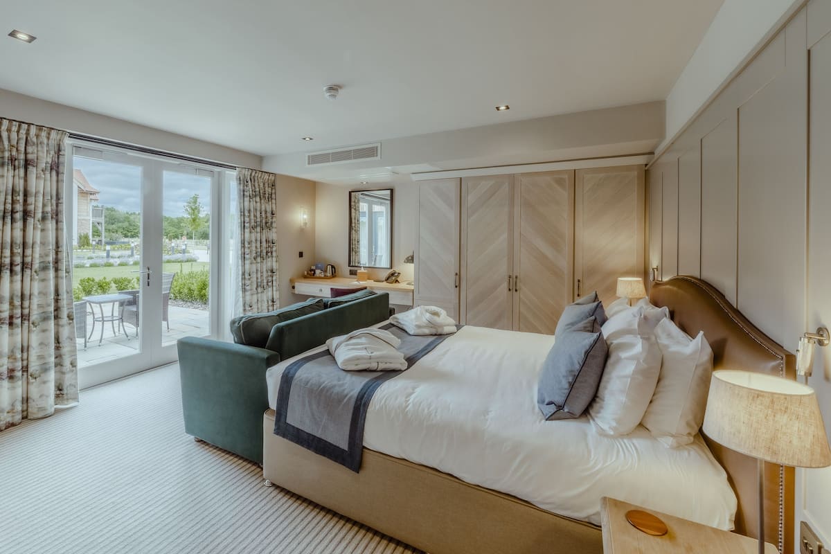 Quarto de hotel moderno com uma cama grande, uma escrivaninha e vista do jardim através da porta de vidro.