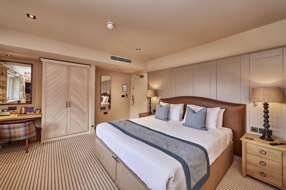 Quarto de hotel com uma cama grande, uma escrivaninha com cadeira, um guarda-roupa e um espelho.