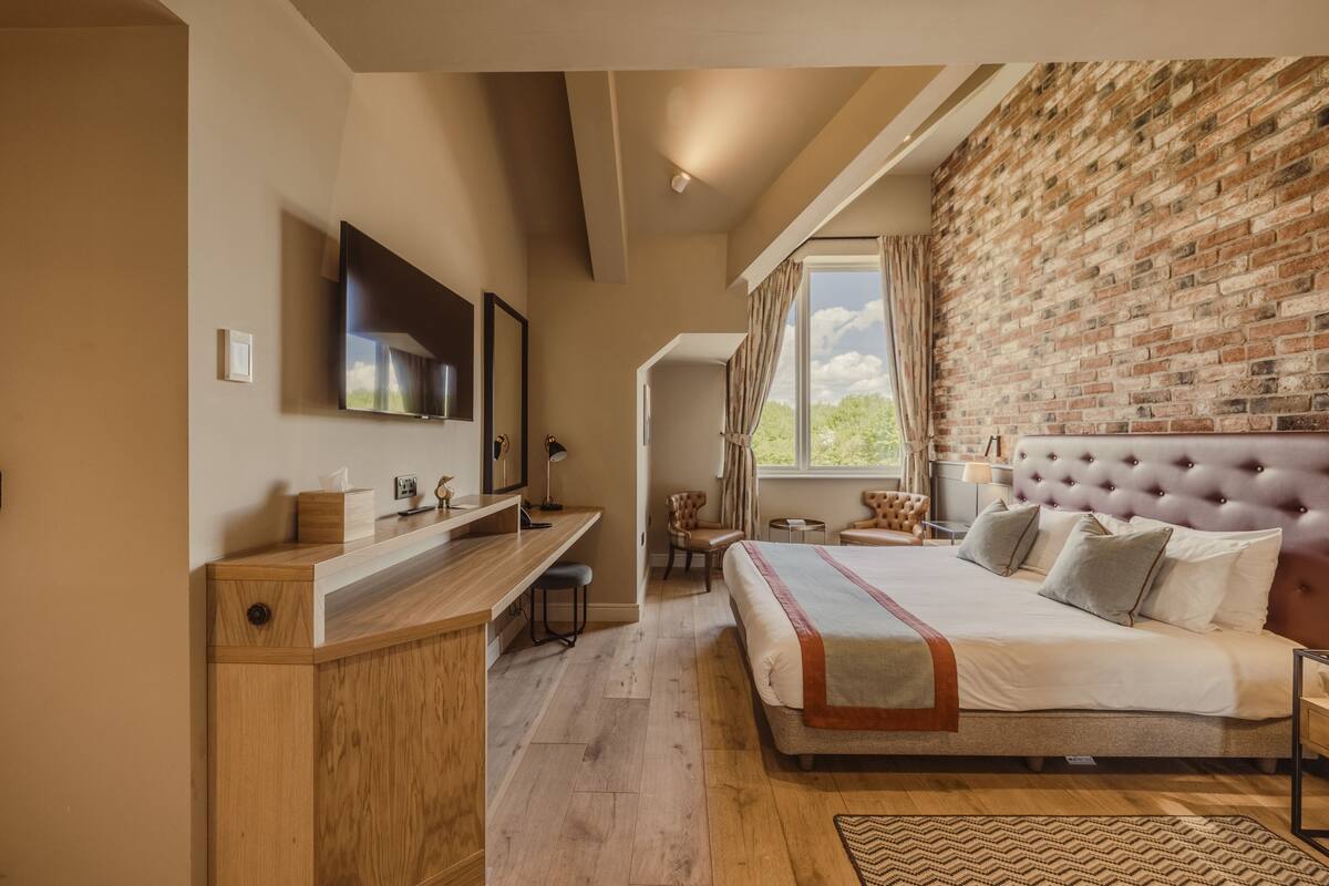 Quarto com cama, escrivaninha, televisão e parede de tijolos.