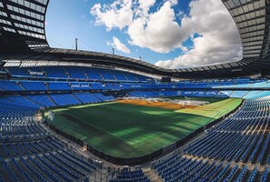 Um estádio grande e vazio, com arquibancadas escalonadas e campo verde.