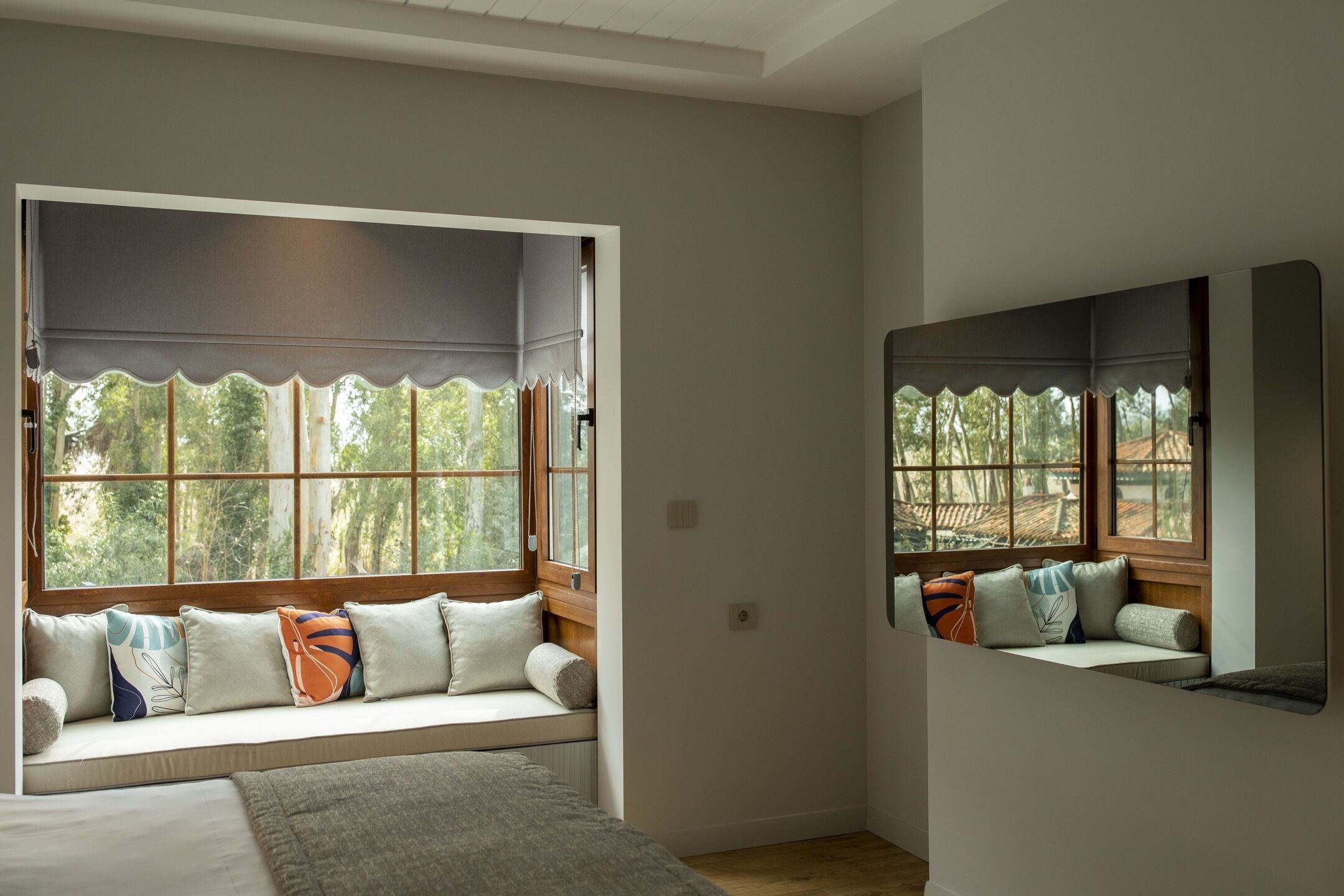 Quarto com um banco embutido junto à janela, uma cama e um espelho.