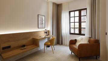 Quarto moderno com escrivaninha de madeira, poltrona confortável, sofá e uma janela grande com cortinas.