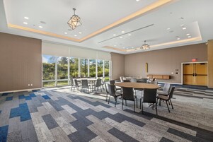 Uma sala de conferências moderna com uma mesa grande e cadeiras, janelas amplas e piso coberto de carpete.