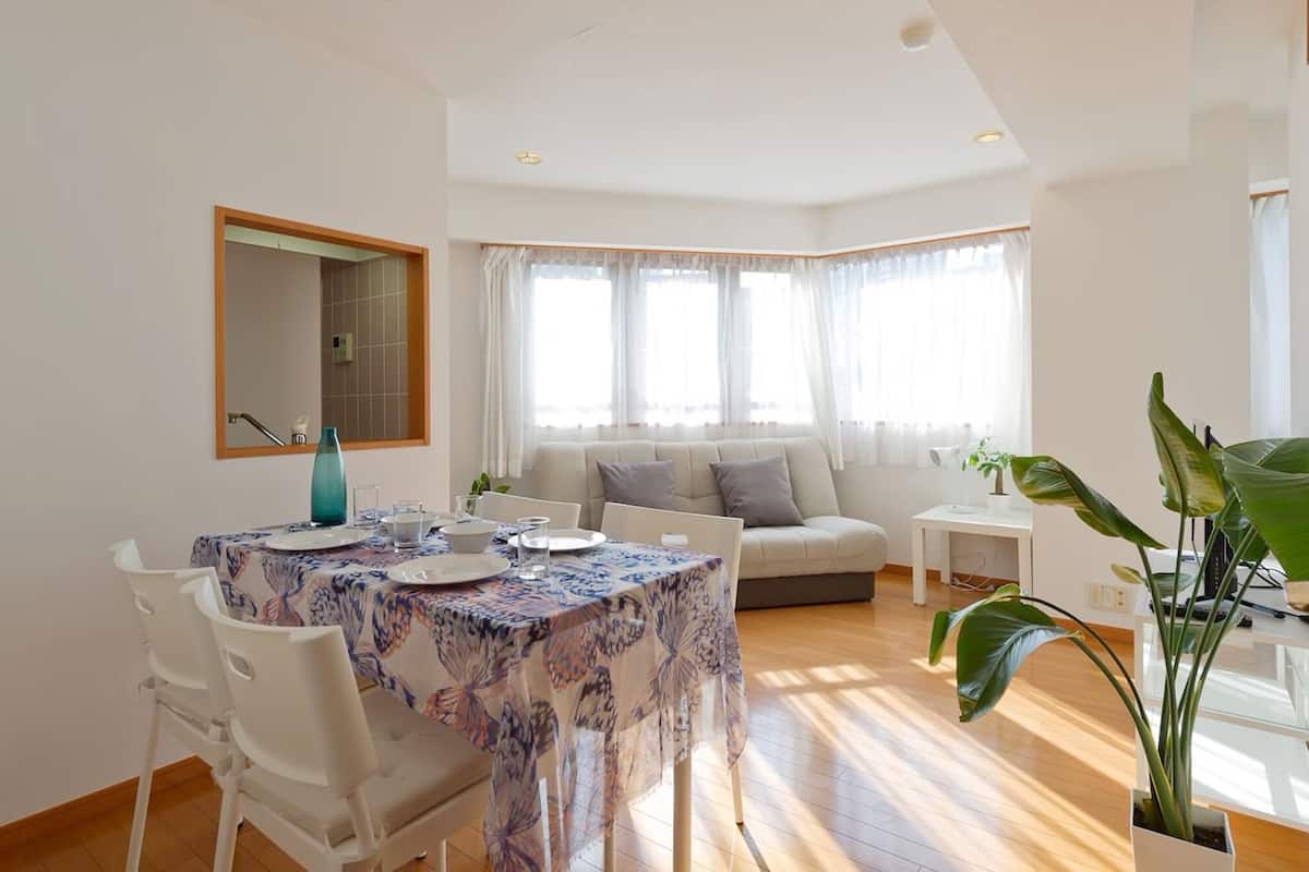 Uma área de refeições com uma mesa posta para quatro pessoas, um sofá e uma janela grande com cortinas.