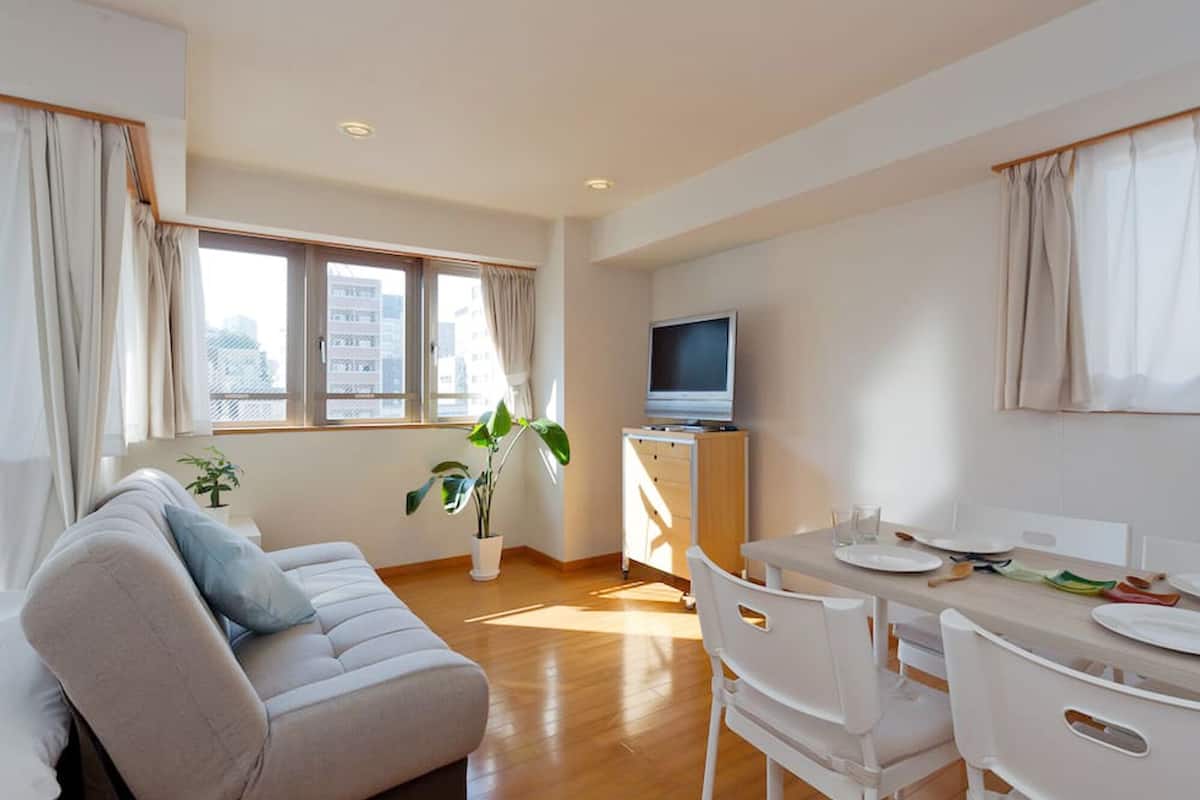 Uma sala de estar moderna com um sofá, mesa de jantar, cadeiras, uma TV e uma planta.