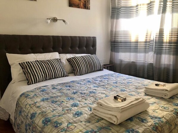 Uma cama bem arrumada com um edredom floral, duas almofadas e um abajur.