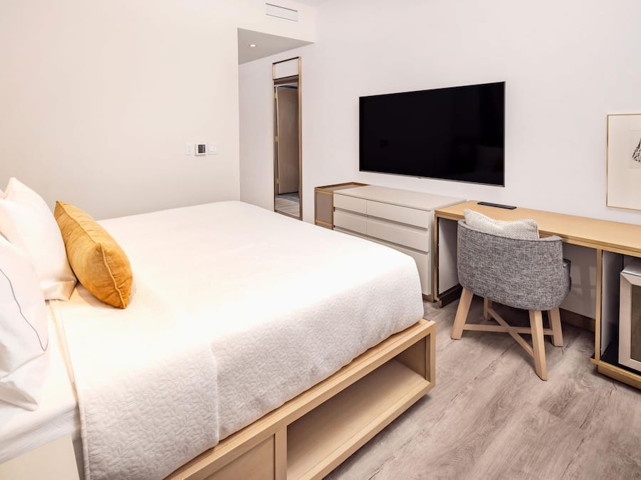 Quarto com cama, escrivaninha, cadeira e televisão.