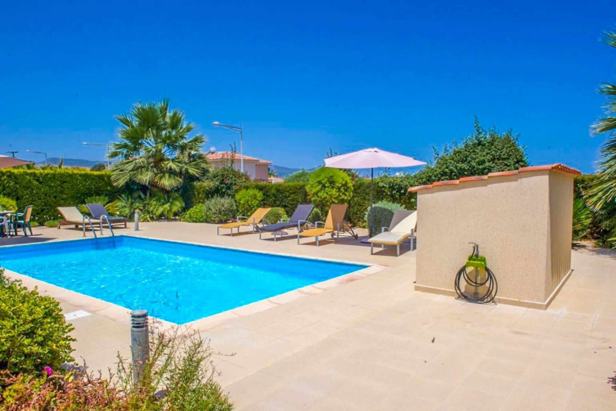 Piscina com espreguiçadeiras e guarda-sóis, rodeada por vegetação e um céu claro.