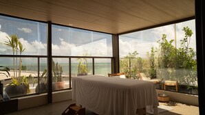 Quarto com cama grande, teto de madeira e vista para o oceano através de amplas janelas.