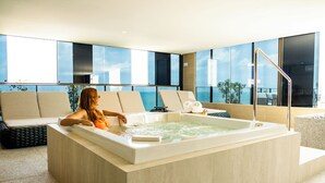 Uma área de spa com uma banheira grande, assentos acolchoados e vista para o mar.