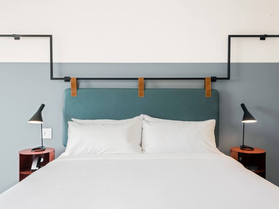 Uma cama com cabeceira azul-turquesa, roupa de cama branca e duas mesas de cabeceira com abajures.