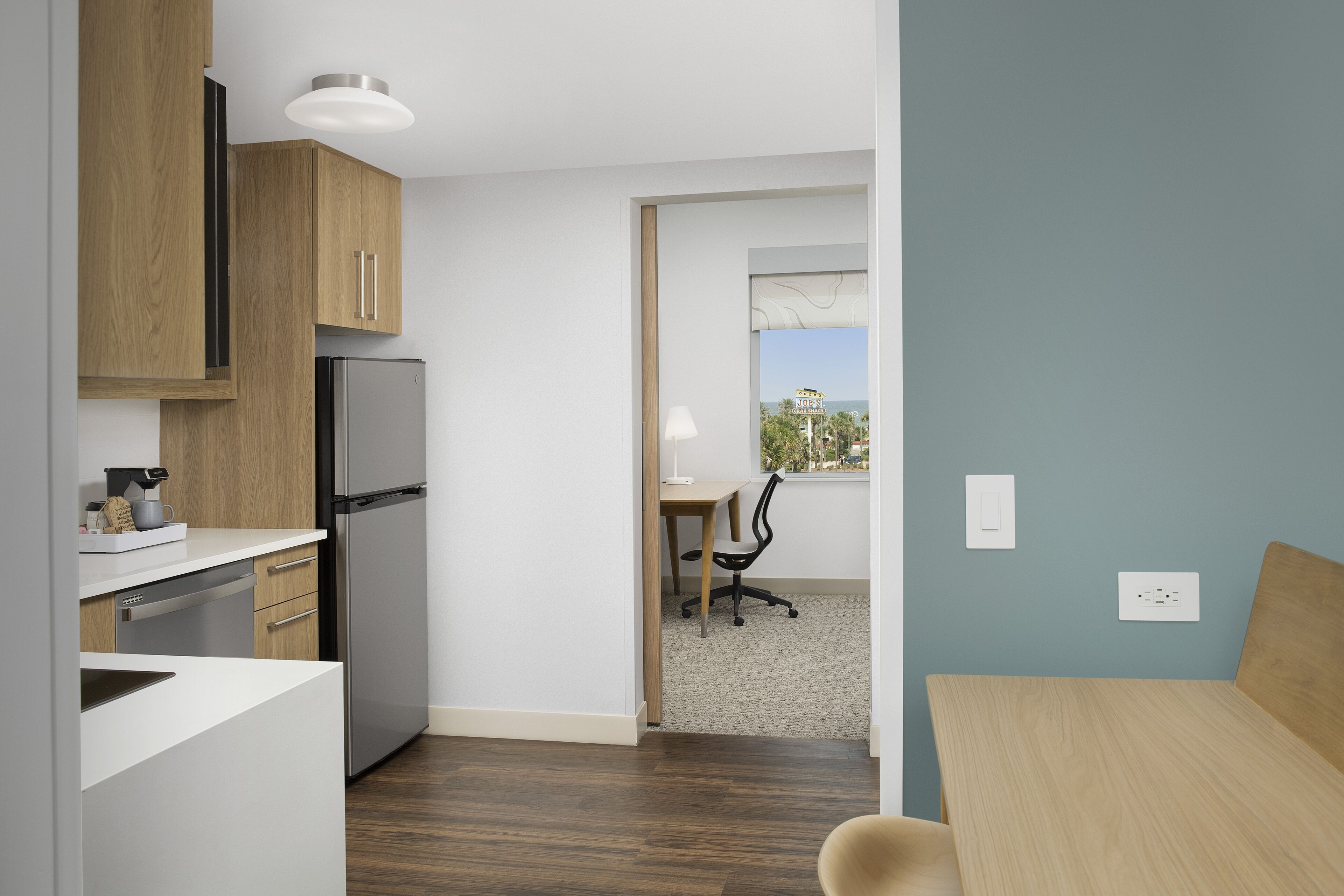 Uma cozinha moderna com geladeira de aço inoxidável, armários de madeira e bancada branca.