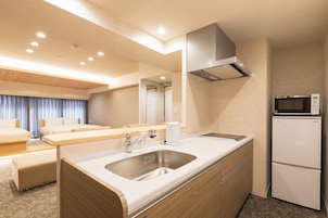 Quarto de hotel moderno com cozinha compacta, pia, micro-ondas, cama de casal e uma grande janela com cortinas.