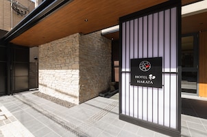 Entrada de hotel com fachada de pedra, placa com o nome do hotel e design moderno com teto de madeira.