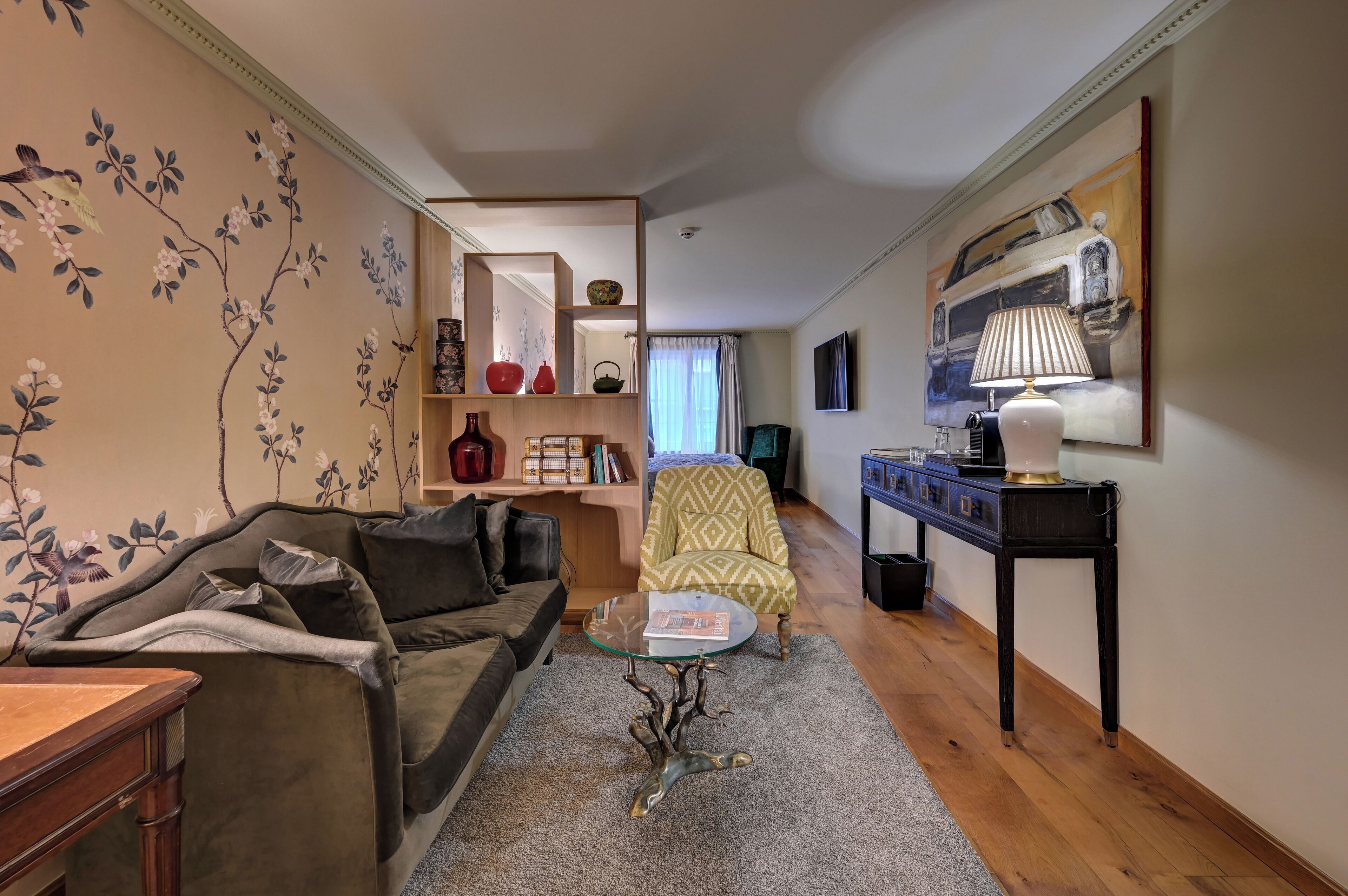 Sala de estar com sofá, poltrona e mesa de centro de vidro. Há um espelho, um abajur e um quadro na parede.