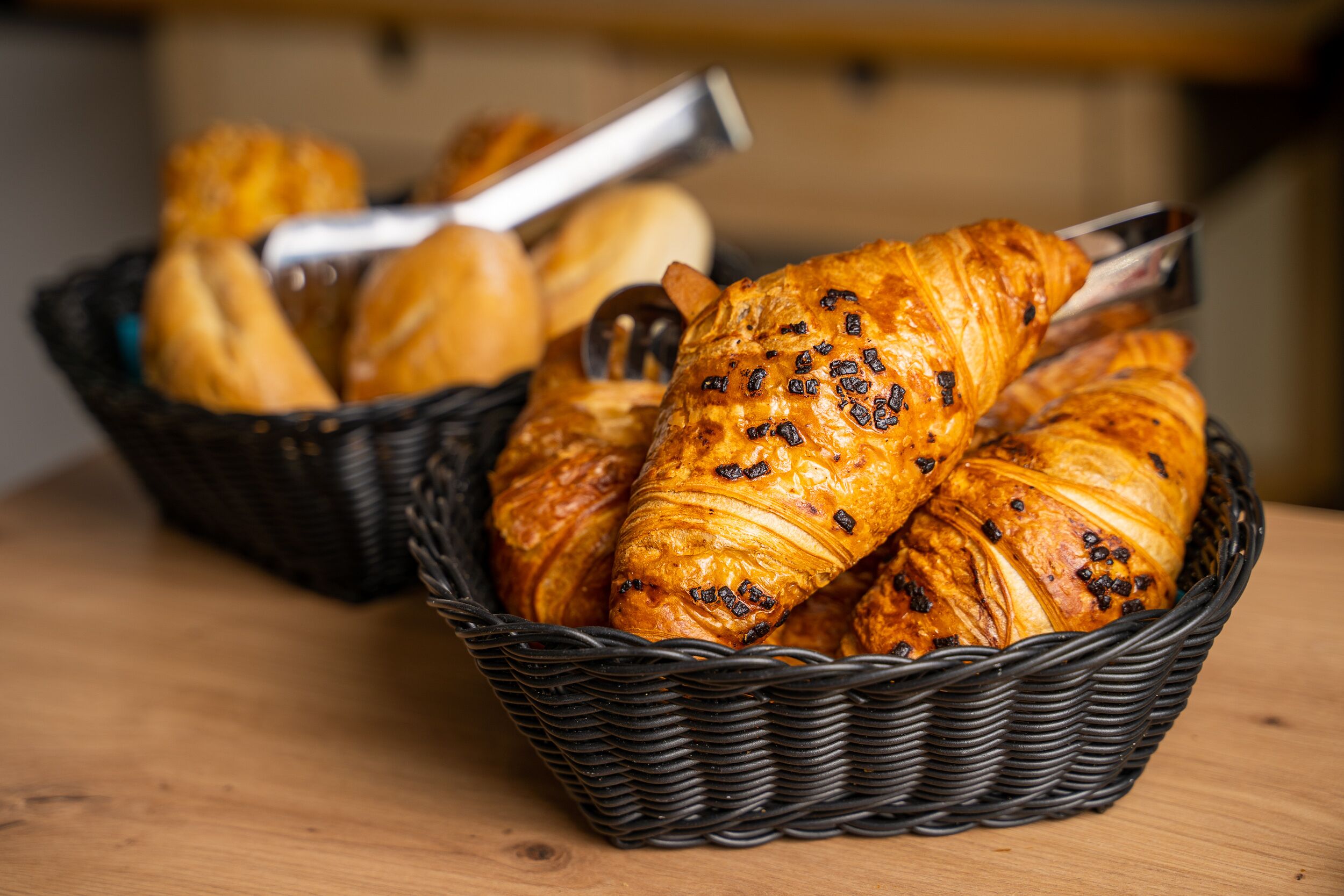 Uma cesta de croissants e uma cesta de pães numa mesa de madeira.