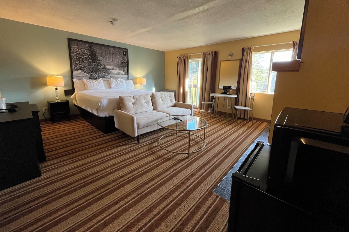 Quarto de hotel com uma cama grande, um sofá, uma mesinha, uma televisão e uma escrivaninha.