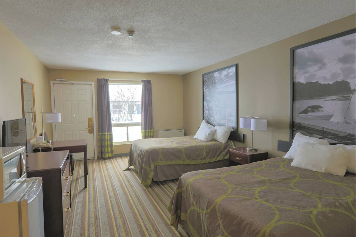 Quarto de hotel com duas camas, uma escrivaninha, televisão e uma janela grande com cortinas.