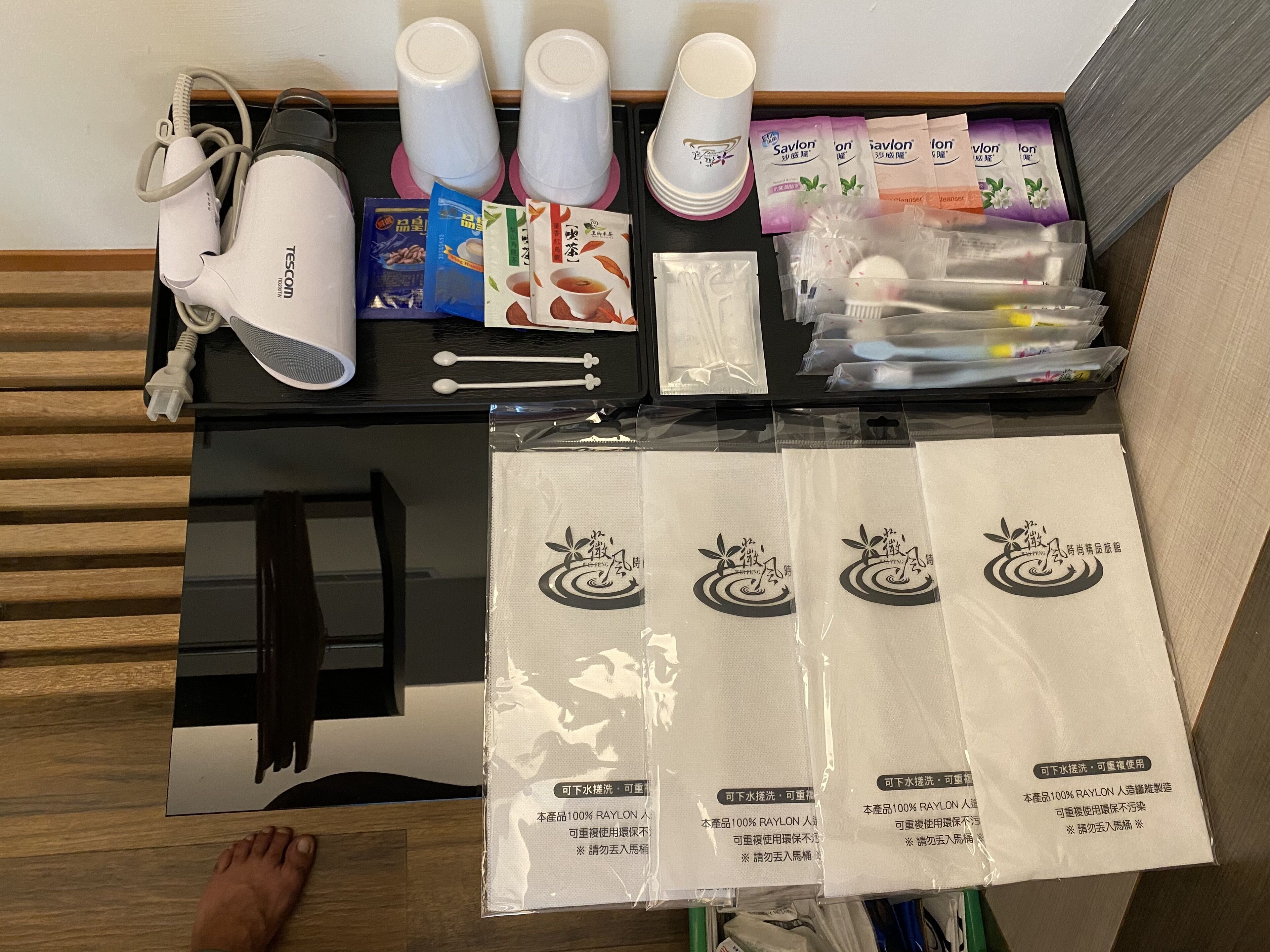 Uma mesa com diversos objetos, incluindo um secador de cabelo, cháquis, pacotes de chá e lenços de papel.