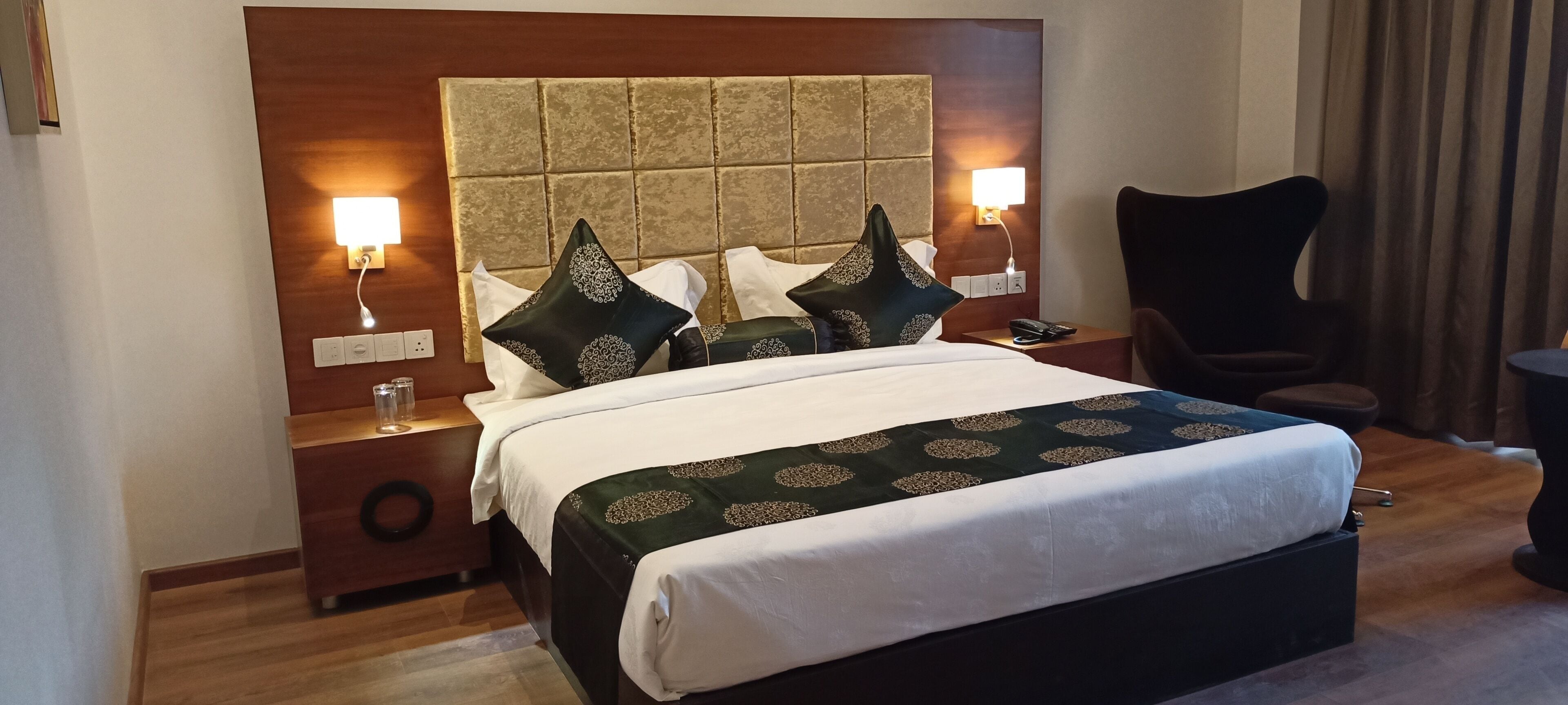 Quarto de hotel com uma cama grande, duas luminárias de cabeceira, uma cadeira e uma mesa de cabeceira.