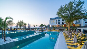 Área de piscina de hotel com várias piscinas, espreguiçadeiras e guarda-sóis.