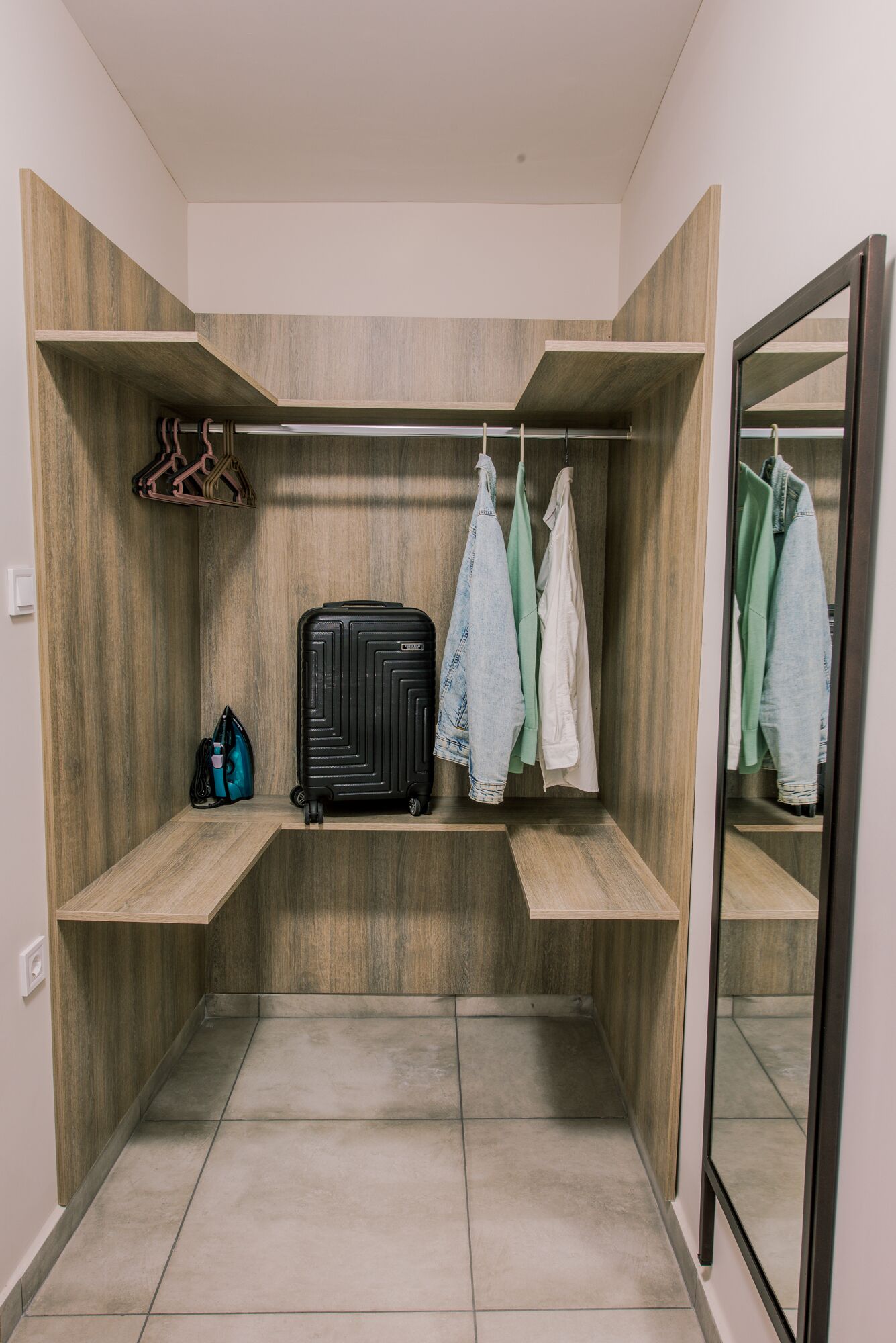 Quarto compacto com roupeiro embutido, mala e roupas penduradas.