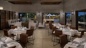 Restaurante com mesas montadas para refeições, área de sofás e grandes janelas com vista para o exterior.