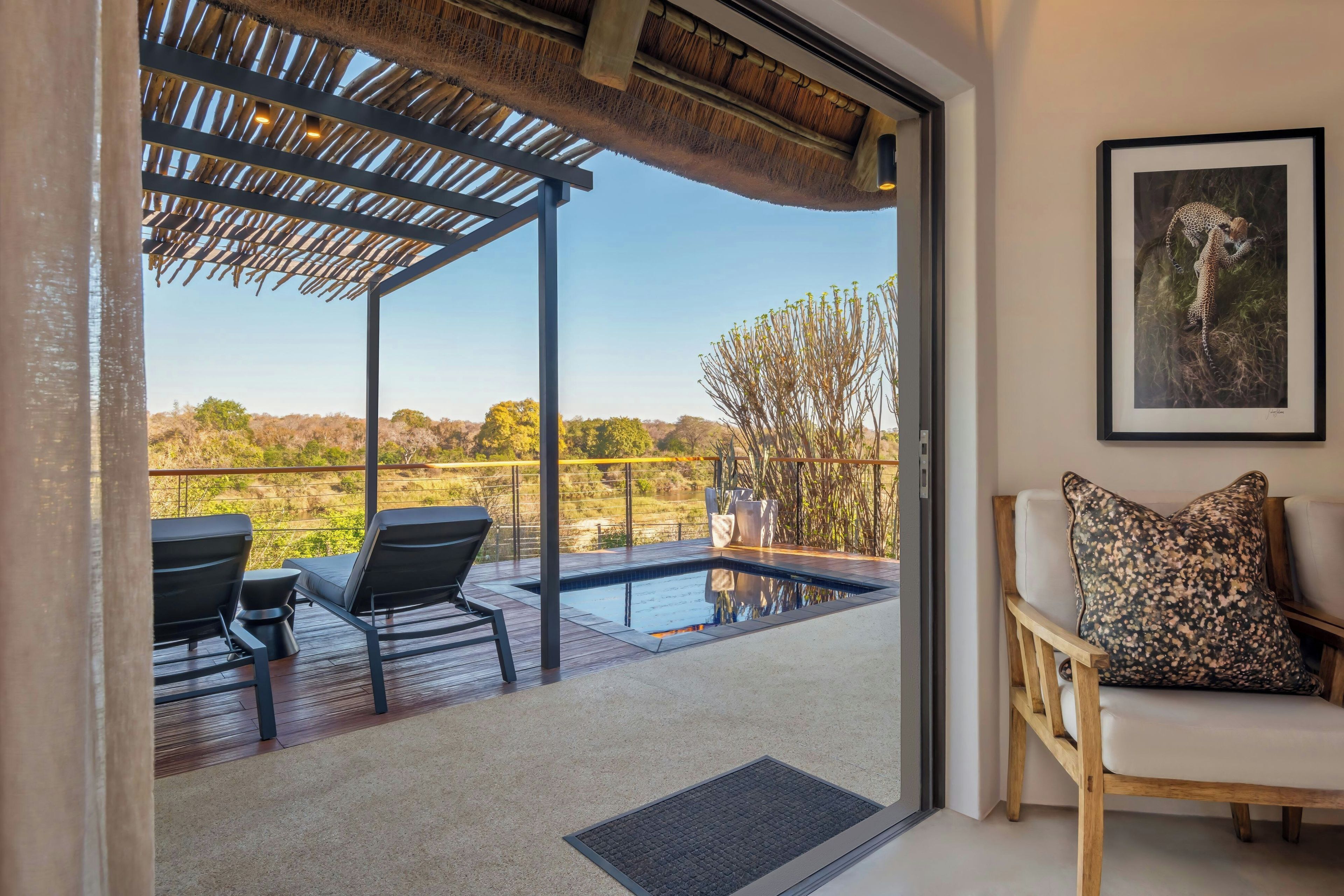 Uma área externa moderna com mobiliário, piscina, alpendre coberto e vista para a paisagem.