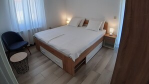 Quarto bem arrumado com cama, mesas de cabeceira, uma cadeira e uma pequena mesa redonda.