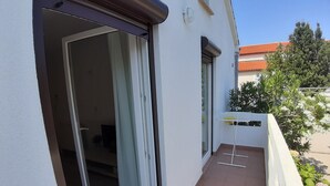 Um edifício residencial com porta de correr de vidro que dá para um espaço interior, uma pequena varanda com mesa de metal e chão em azulejo.