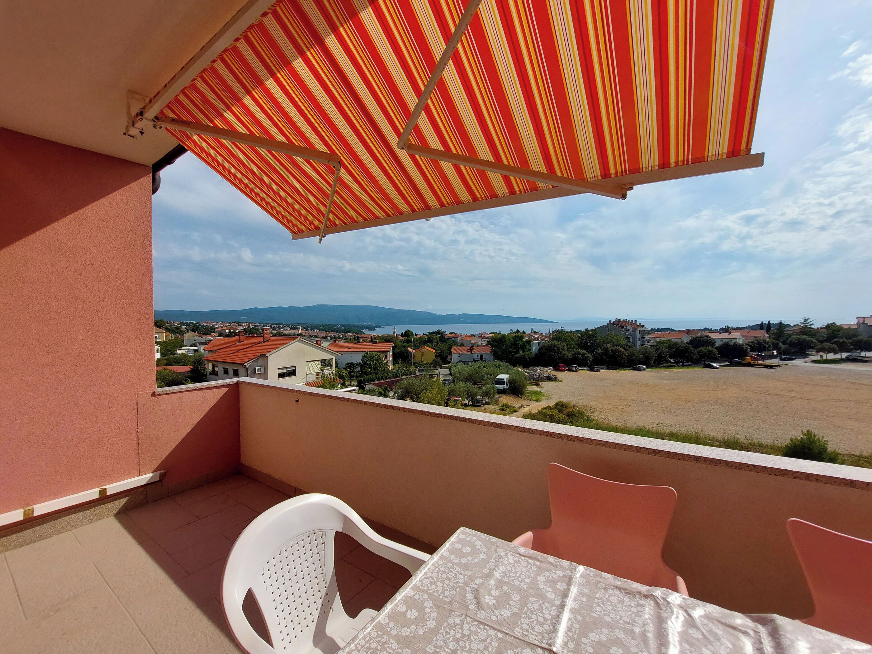 Uma varanda com toldo listrado, uma mesa e cadeiras.