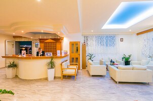 Um saguão de hotel com balcão de recepção, área de estar e um amplo claraboia.