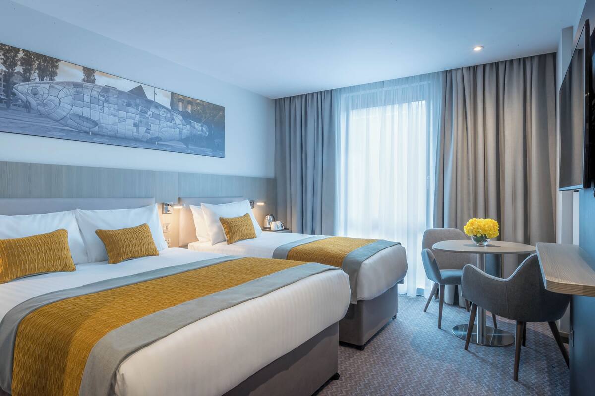 Quarto de hotel com duas camas, uma escrivaninha e uma cadeira.