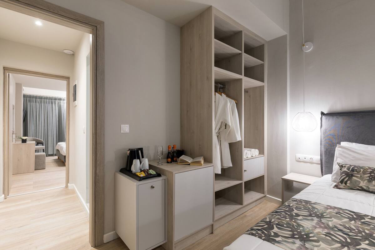 Quarto de hotel moderno com um guarda-roupa grande, uma mesa de cabeceira com um livro e óculos, e uma cama com colcha estampada.