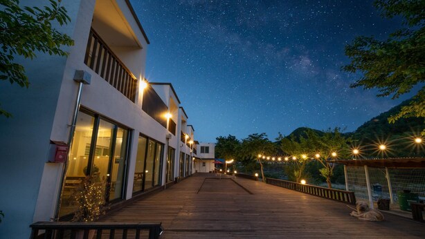 Um edifício moderno com janelas amplas, um deck de madeira e luzes de cordão.
