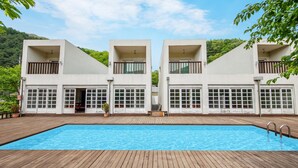 Um edifício moderno com piscina, apresentando um deck de madeira e várias varandas.