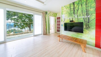 Quarto espaçoso com uma janela grande, televisão de tela plana em um suporte de madeira, e um mural na parede retratando uma cena de floresta.
